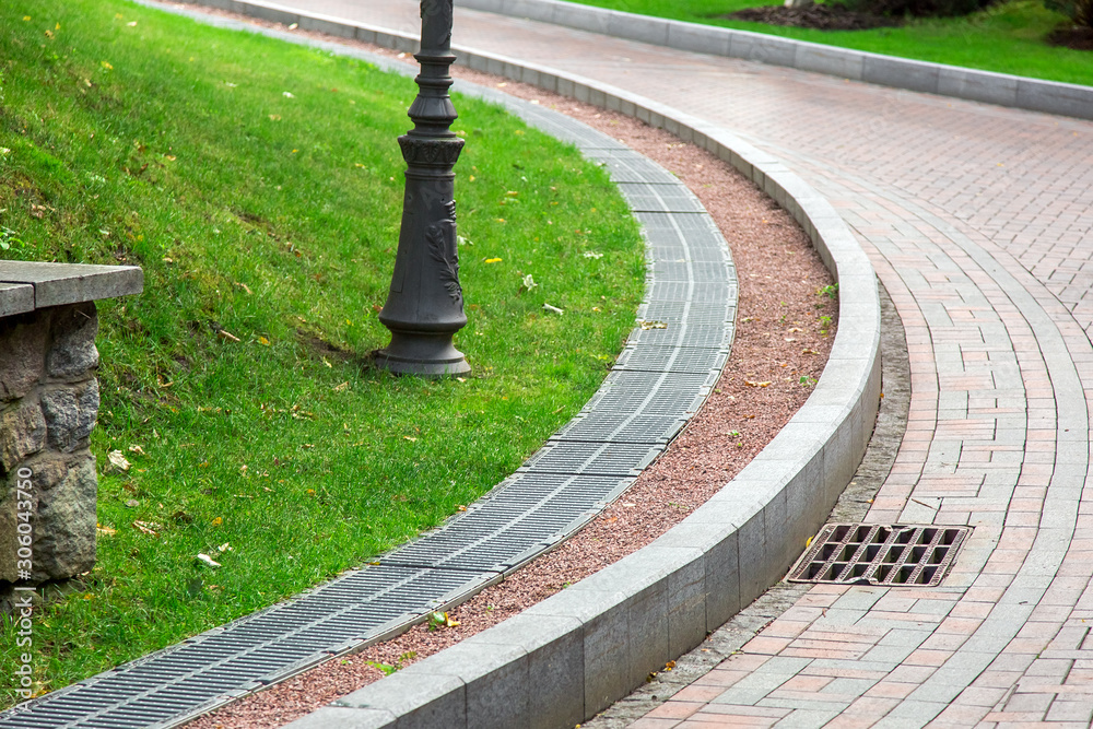 grille of the drainage system manhole on the curve pedestrian sidewalk ...