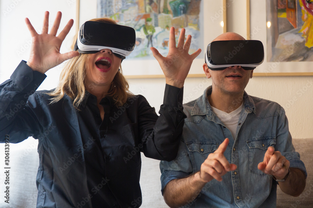 Excited couple wearing VR headset, shouting and touching air. Middle ...