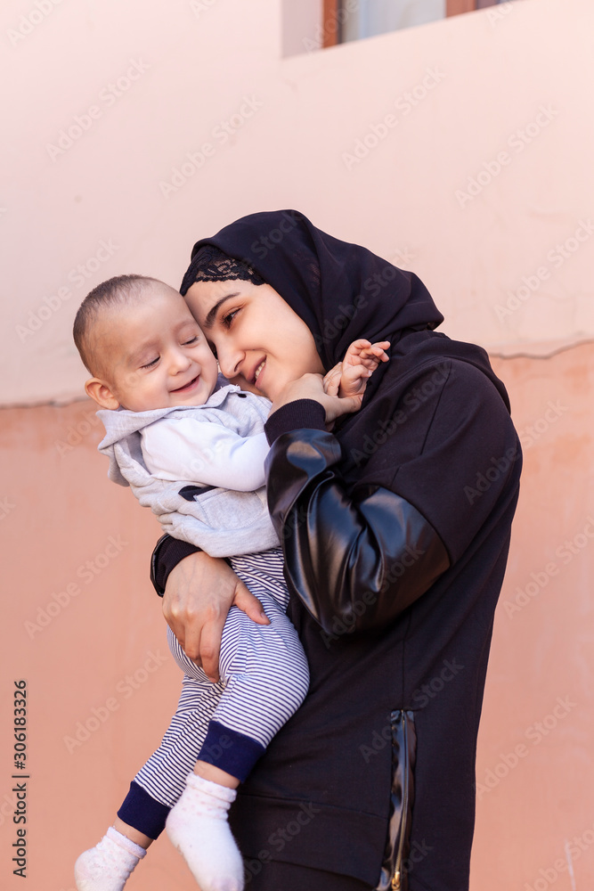 Young Muslim woman in hijab holding her 1-year-old baby boy, hugging ...