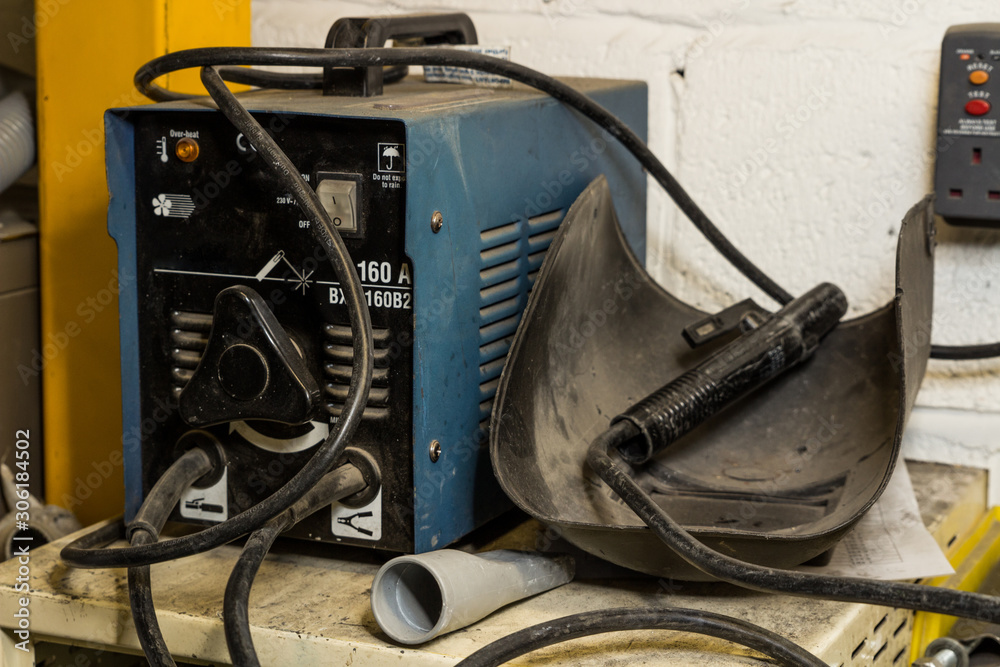 Welding machine on a dirty table with a mask and gun in a factory used ...