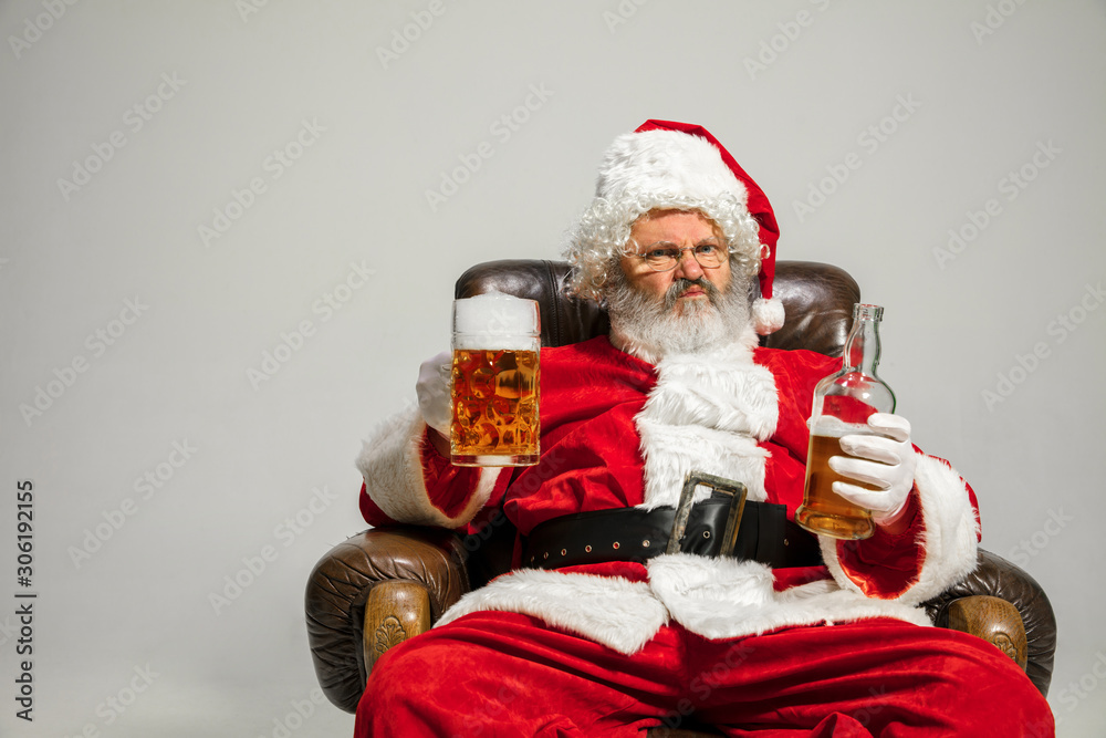 Santa Claus drinking beer sitting on armchair, congratulating, looks ...