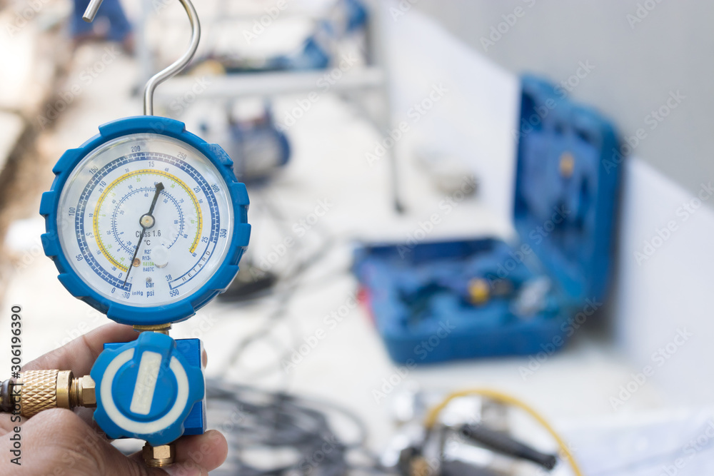 Technicians use manifold gauges to check the refrigerant pressure of ...
