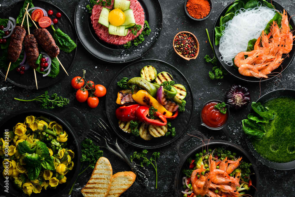 Assorted food and dishes of vegetables, meat and fish on a black stone ...