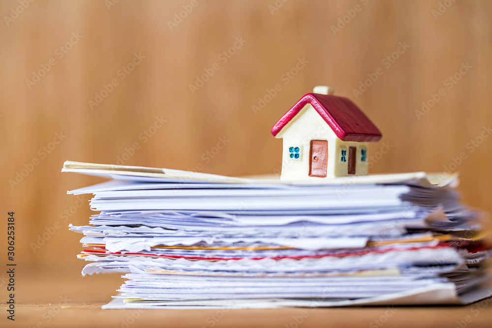 miniature house with red roof on stack of paper over wooden mock up ...