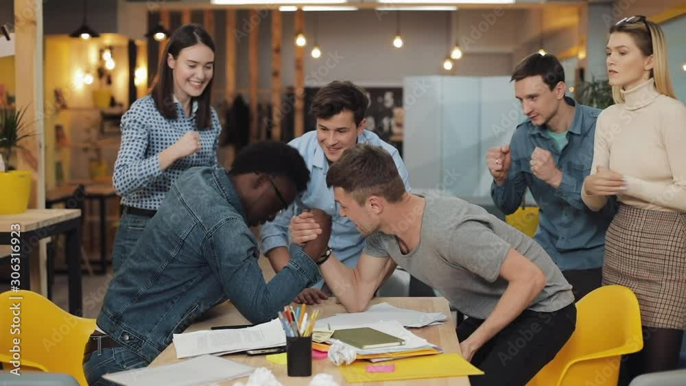 Two young men competing arm wrestling in office. Joyful colleagues ...