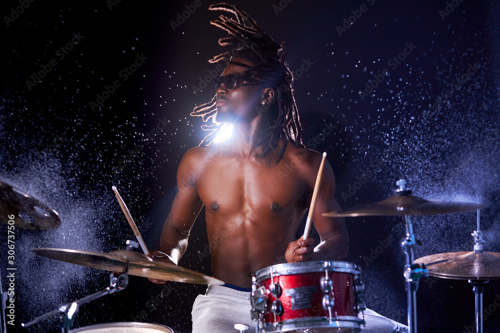 wet drum set covered with water drops, african young man beating on ...
