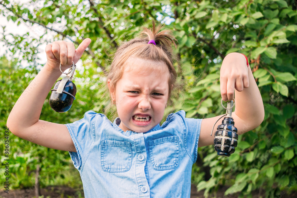 An angry little girl holds two grenades in her hands. Baby hold bombs ...