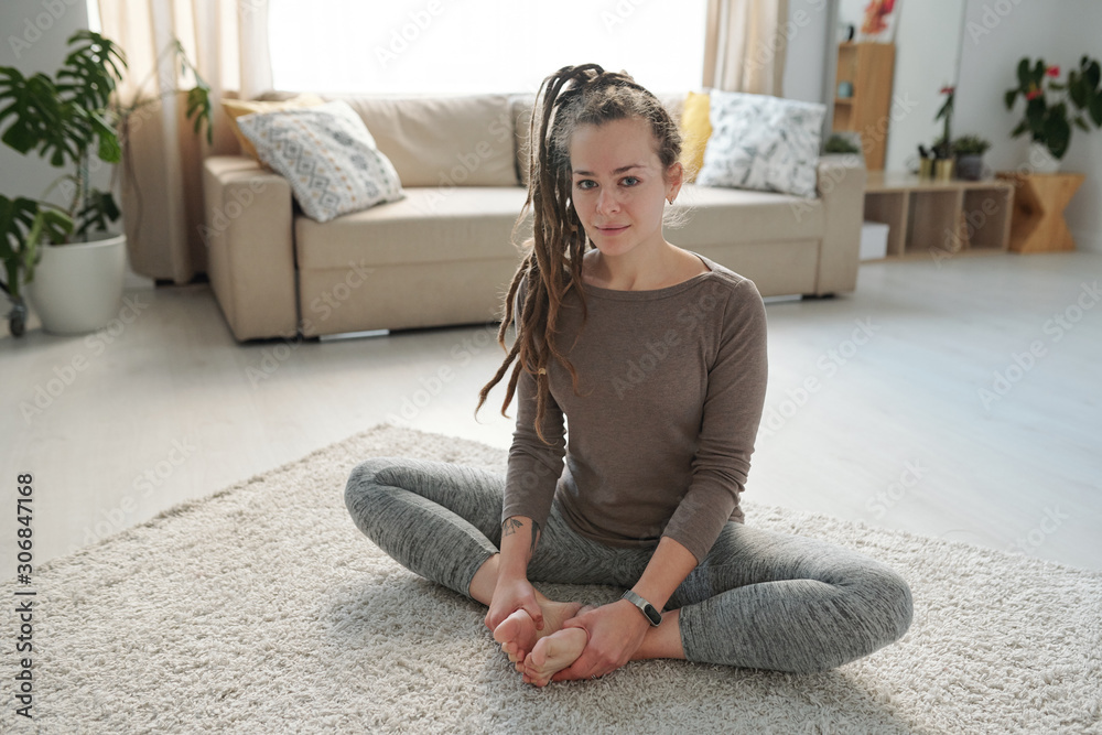 Pretty young active woman putting her bare soles together during yoga ...