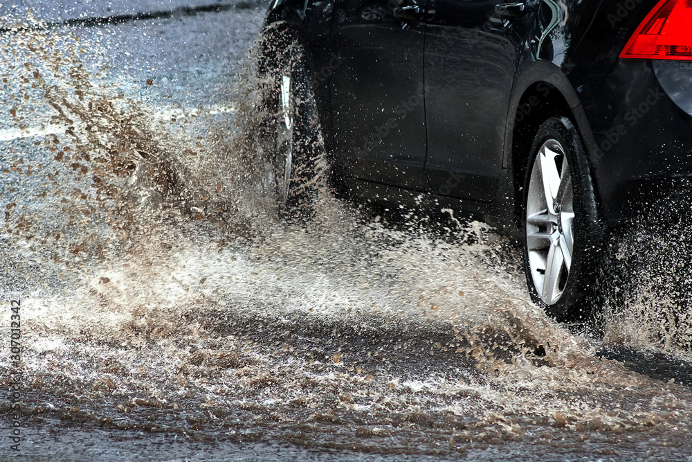 Foto de Car splashes through large puddle on flooded street. Motion car ...
