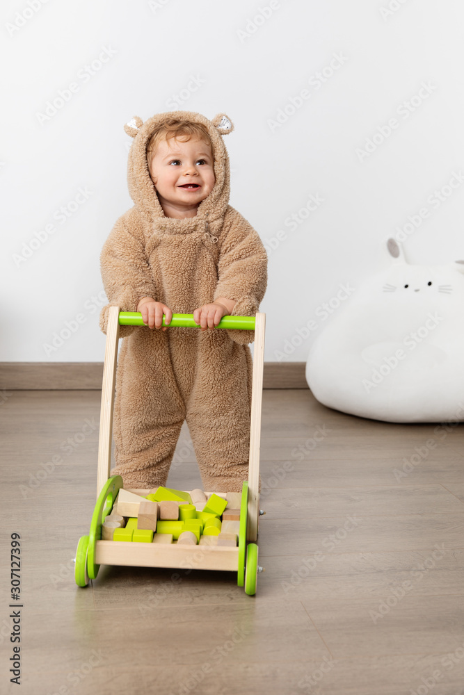 Smiling baby in hooded bear suit learning to walk with trolley Stock ...