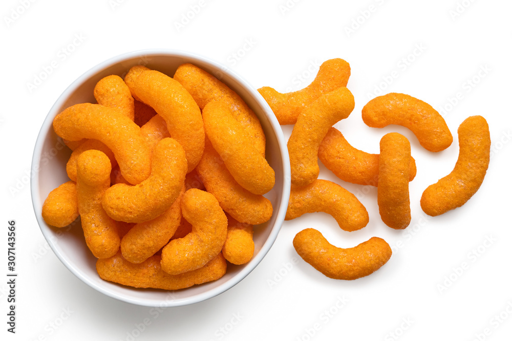 Extruded cheese puffs in a white ceramic bowl next to spilled cheese ...