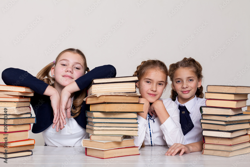 three girls of school girls with books for study sit at the desk in the ...