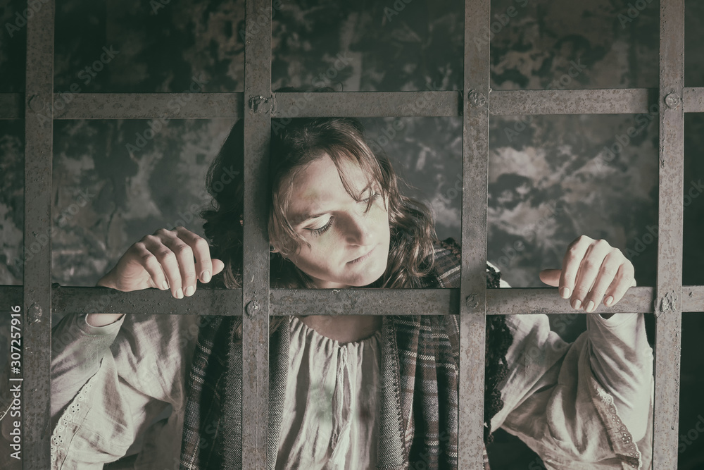 Girl in old clothes sad on the background of a prison cell and retro ...
