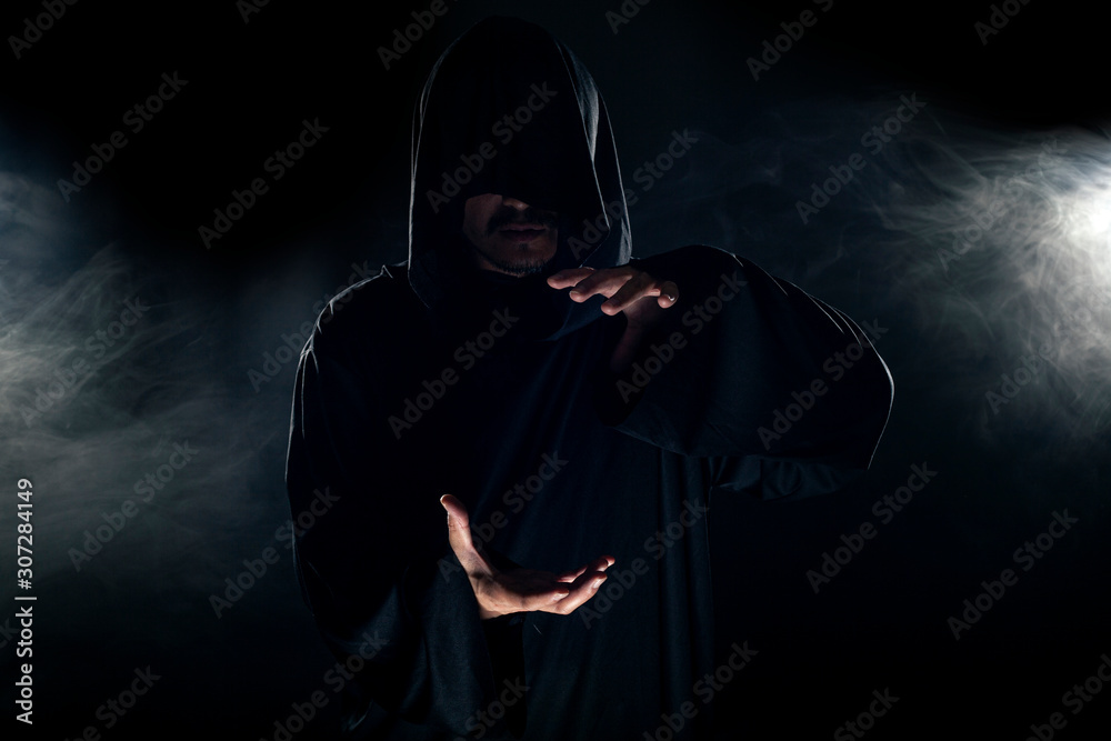 Man dressed in a dark robe looking like a cult leader on a smoky or ...