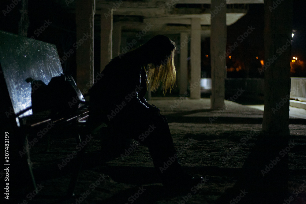 dark silhouette of a sad girl sitting on a bench in a depressive pose ...