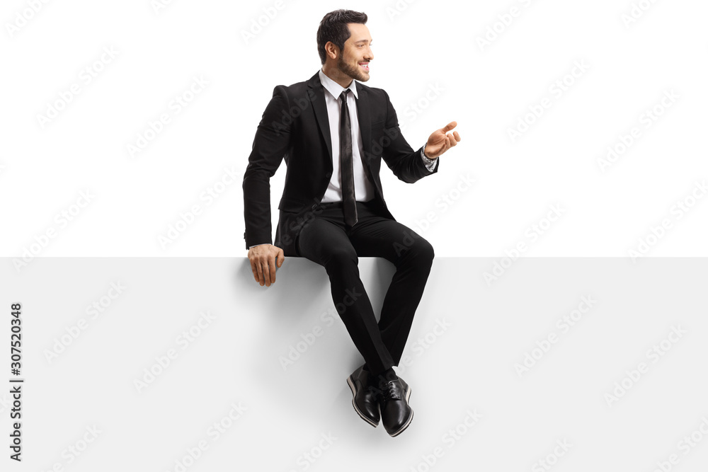 Handsome young man in a suit sitting on a blank panel and gesturing ...