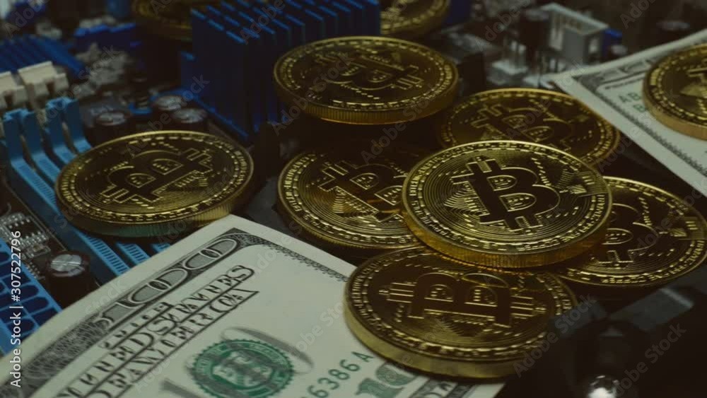 Bitcoin gold coin rotates on a computer motherboard. 100 dollar bills ...