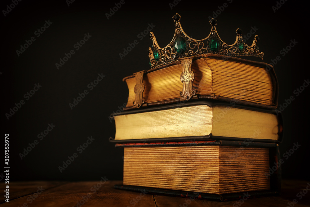 low key image of beautiful queen/king crown over old book and wooden ...