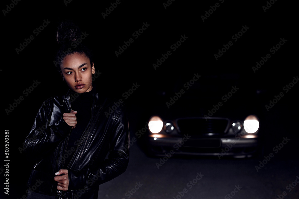 a young mulatto girl in a leather jacket and black clothes poses on an ...