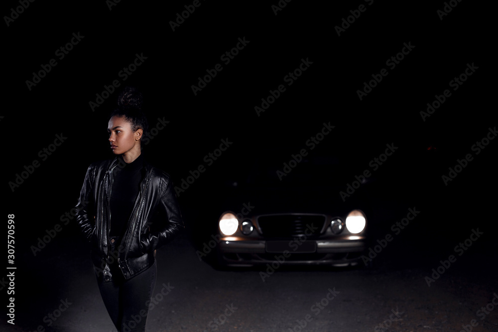 a young mulatto girl in a leather jacket and black clothes poses on an ...