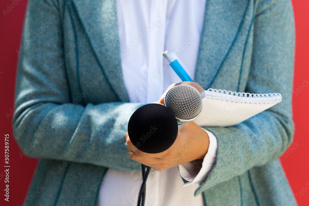 Female journalist at news conference, writing notes, holding microphone ...