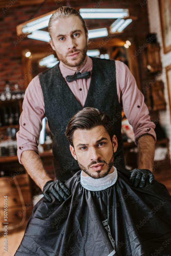 handsome barber in latex gloves putting hands on shoulders of man in ...
