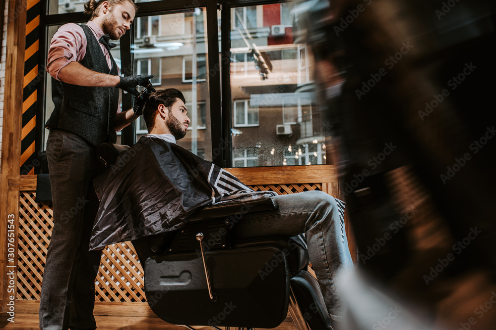 side view of handsome barber styling hair of bearded man in modern ...
