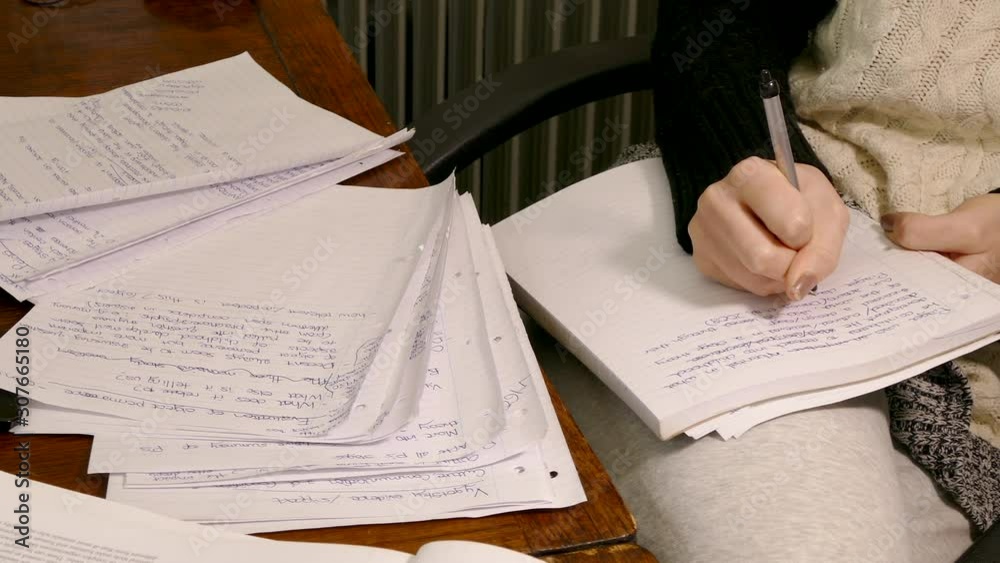 Close dolly shot of a young woman student’s hand using a pen to write ...