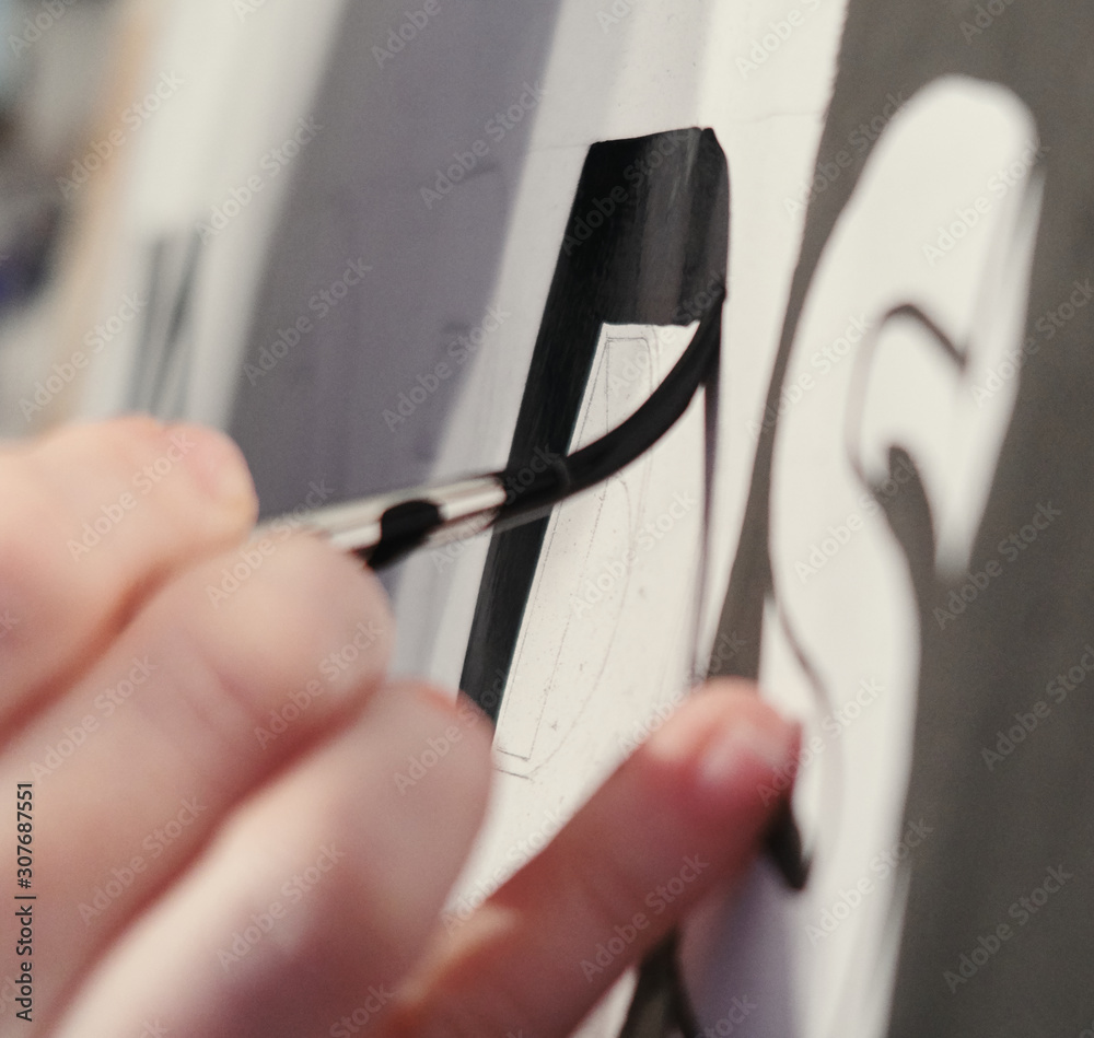 An artists hand with a paint brush painting retro letters and ...