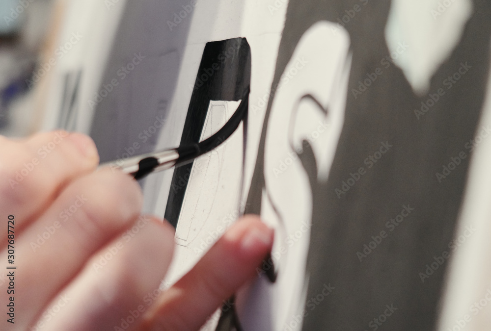 An artists hand with a paint brush painting retro letters and ...