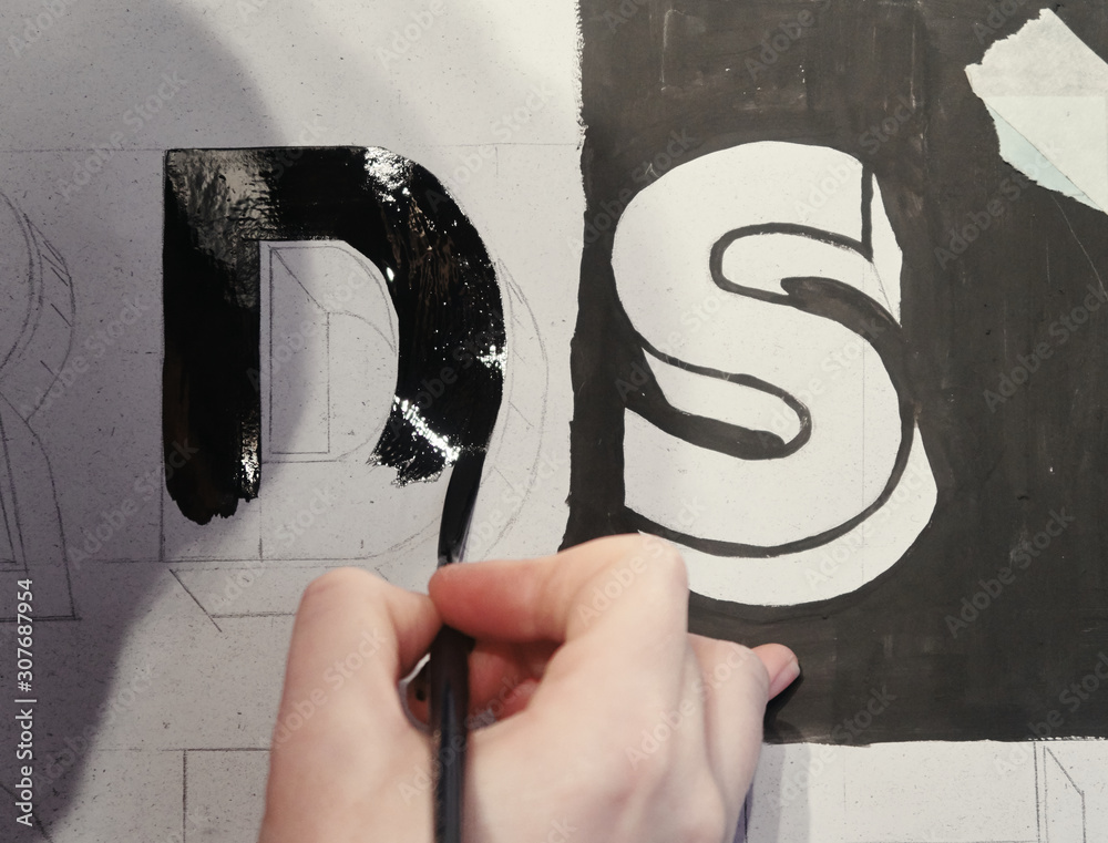An artists hand with a paint brush painting retro letters and ...