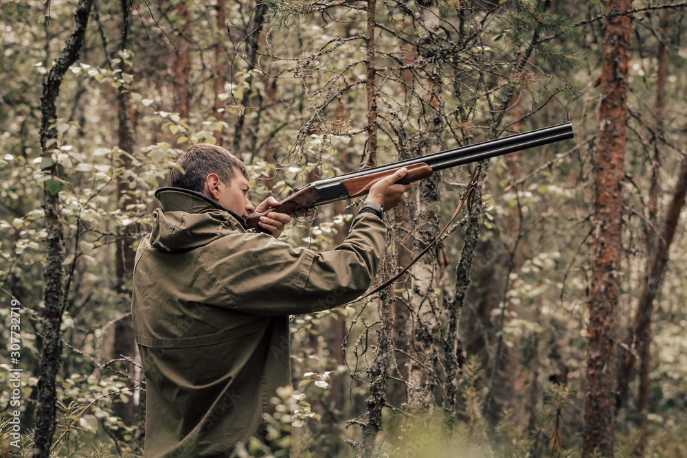 Hunter with shotgun and hunting form on hunt in forest. Armed man is ...