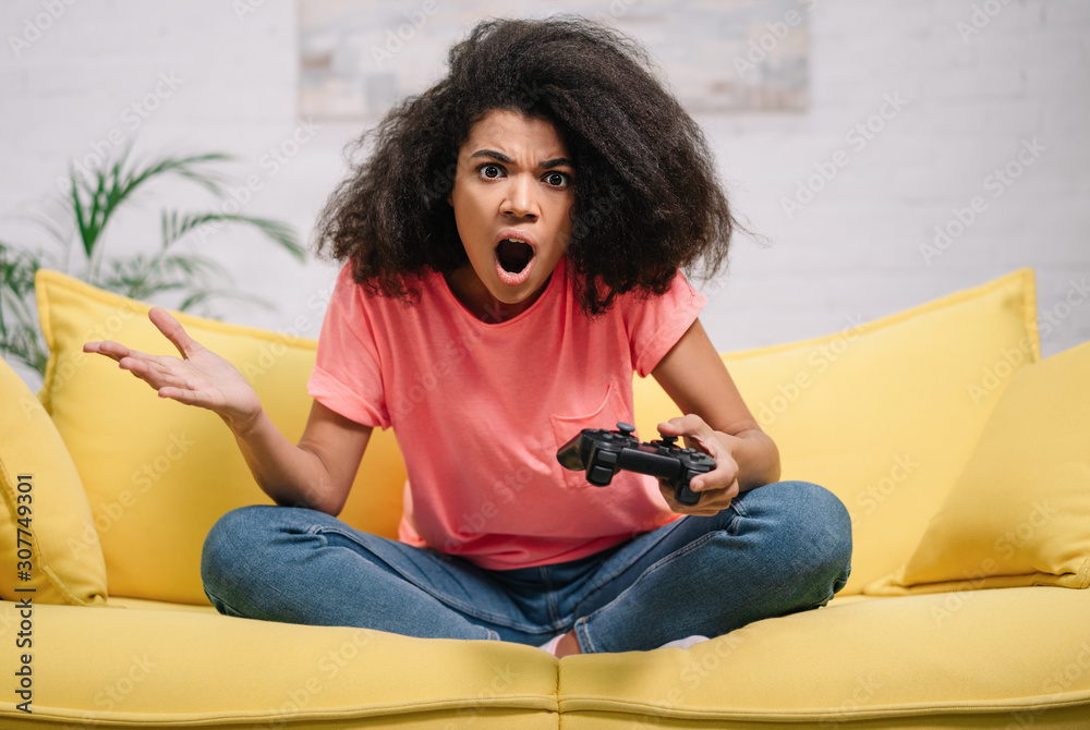 Emotional Woman Playing Video Games Sitting On Yellow Sofa Holding Wireless Joystick Excited