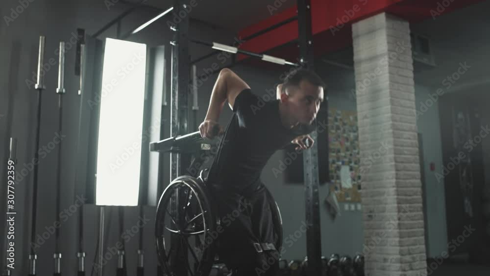 Workout, young disabled athlete in wheelchair performs push-ups on bars ...