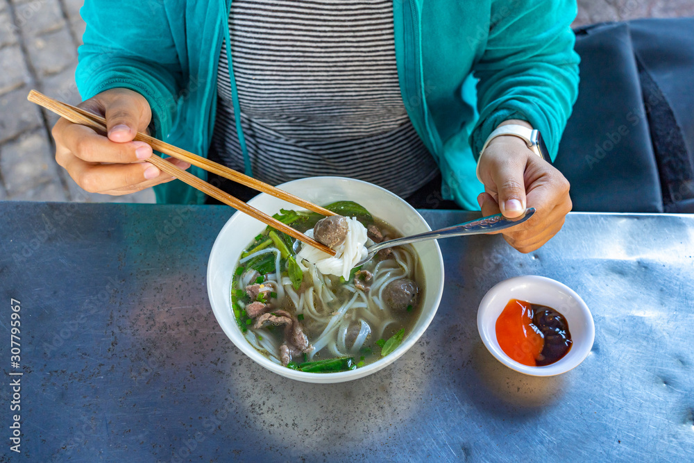 Female traveler eating famous Vietnamese food- Pho beef noodle soup ...
