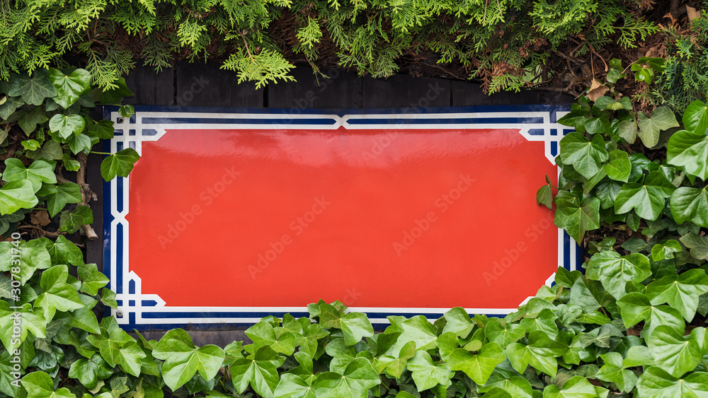 Red rectangular metal sign board bordered by leaves of common ivy and ...