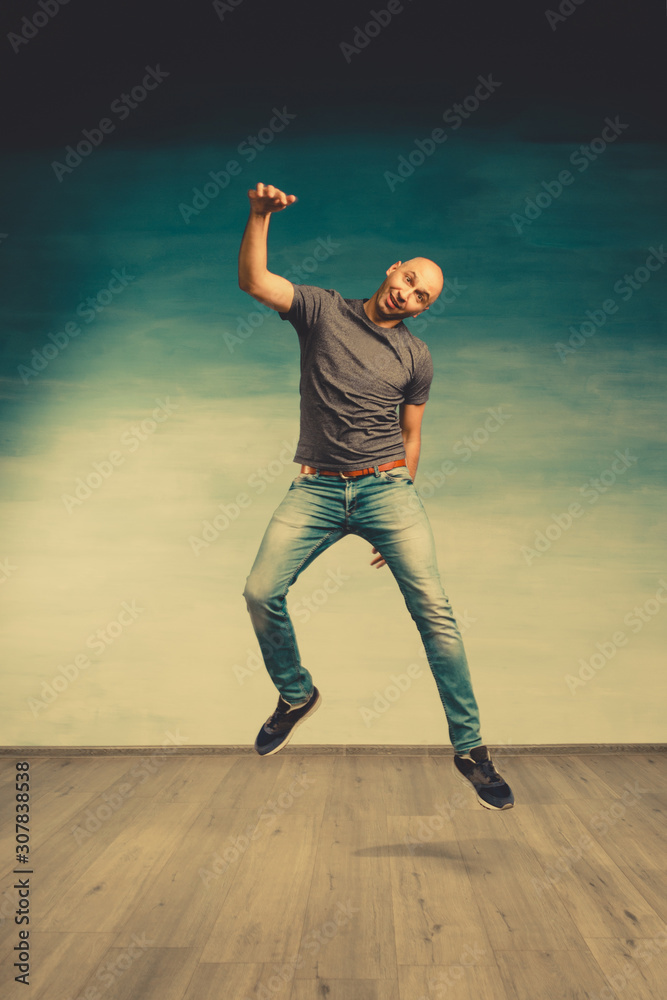 Cool bald man in a gray T-shirt and jeans jumping and fooling around ...