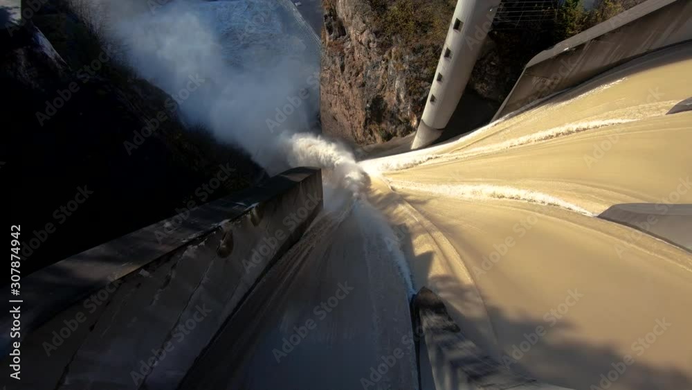 Looking down yellow flooded water flowing over concrete spillway ...