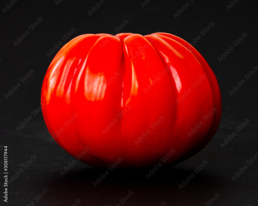 Organic, perfect shape Zapotec tomato, red and ribbed. Side view, black ...