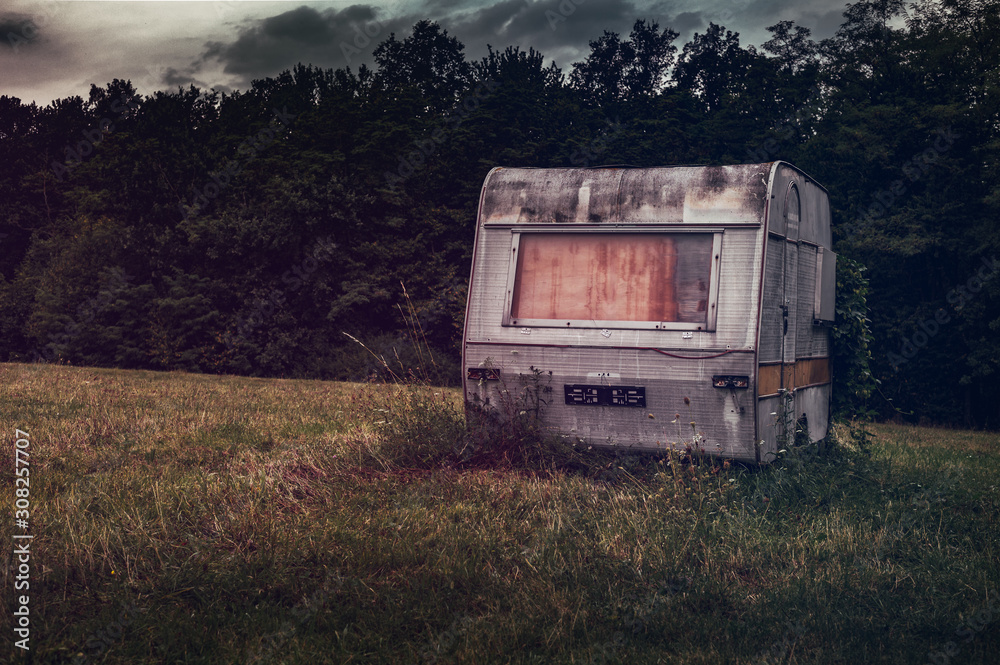 Abandoned and rusty small travel trailer in the meadow with forest on ...