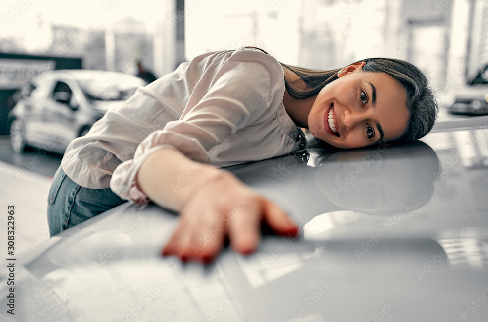Beautiful woman hugging and showing her love to a car in a car showroom ...