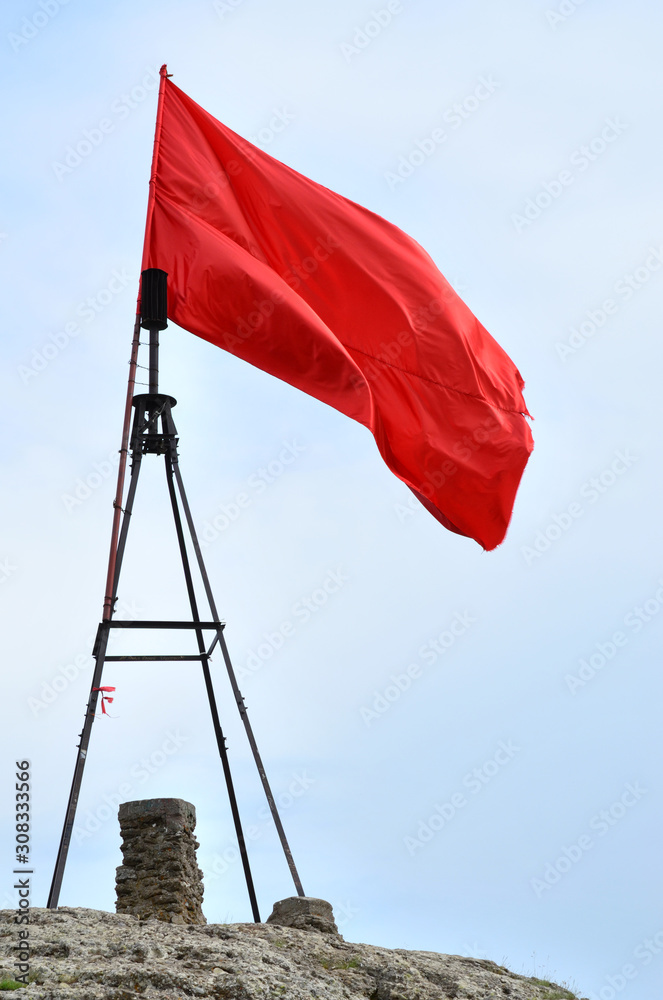 Red flag at the top of high mountain on overcast day. A scarlet banner ...