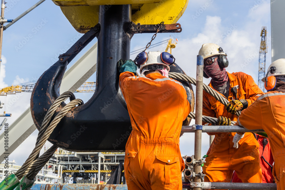 Offshore workers installing a heavy lifting sling onto a crane hook on ...