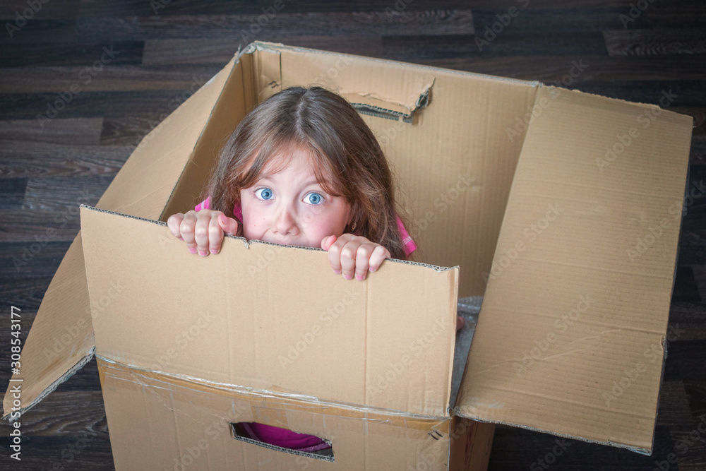 A scared girl peeks out of a cardboard box. The child is hiding from ...