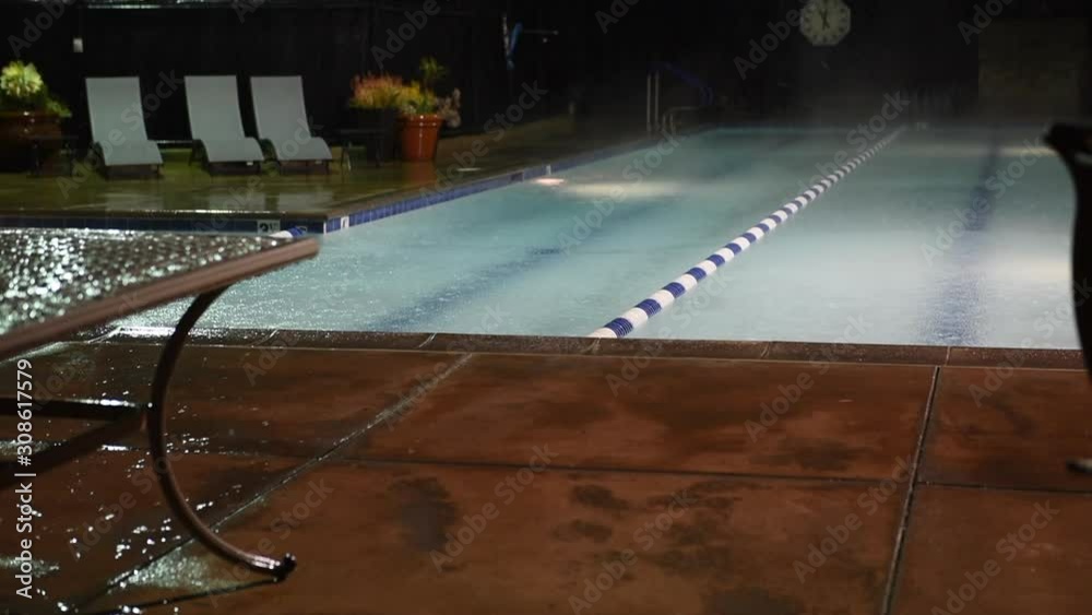 Rain falls steadily into swimming lap pool at night during autumn rain ...