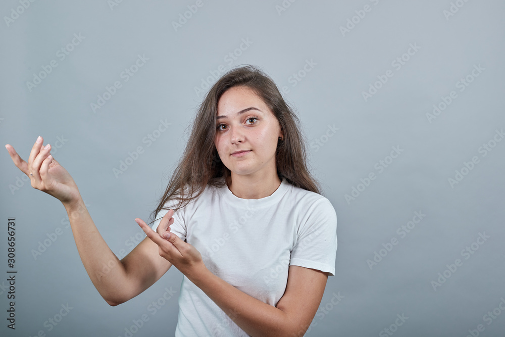 Teen in white t-shirt shows something with two hands that she points to ...