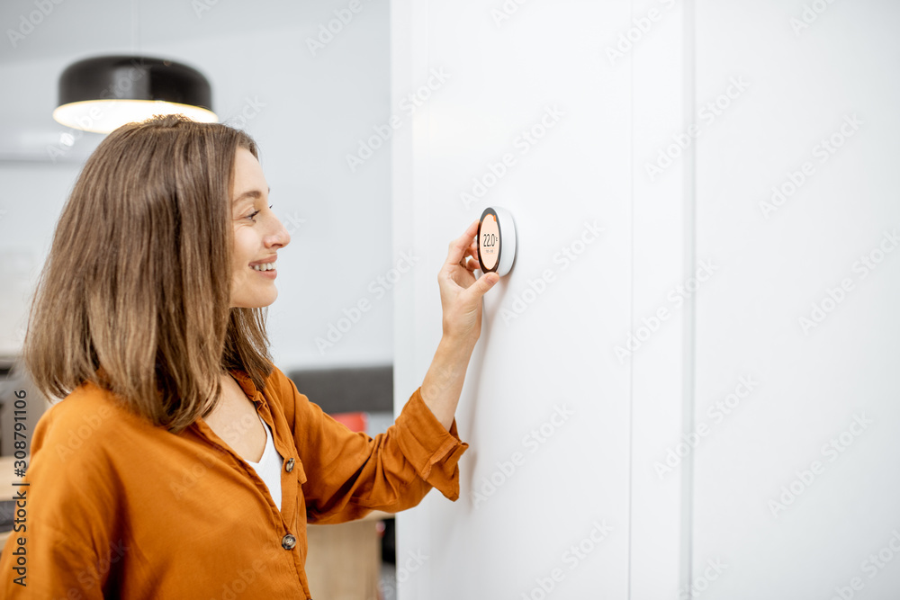 Young woman regulating heating temperature with a modern wireless ...