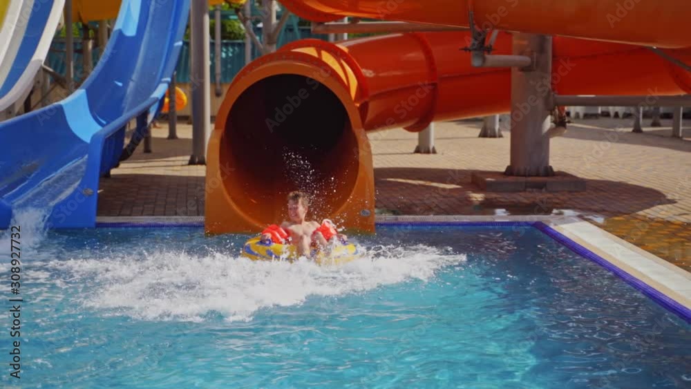 Sliding down on waterslide. Boy playing at waterpark pool going down on ...