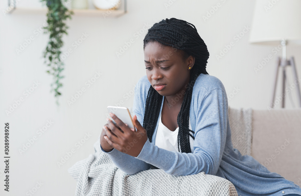 Young black woman looking at smartphone screen with sad face expression ...
