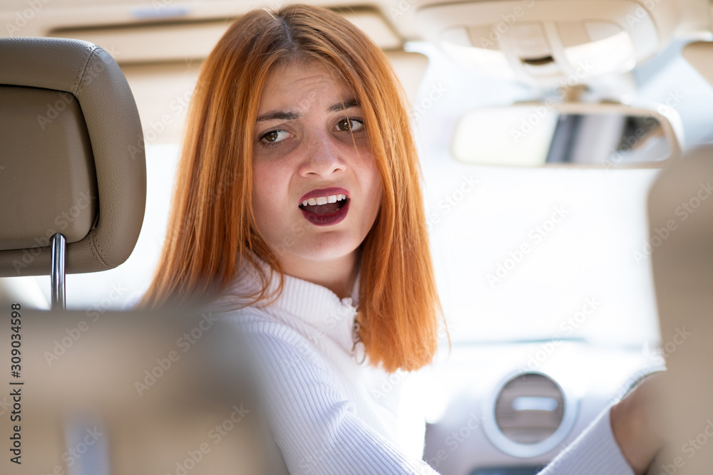Young woman driving a car backwards. Girl with funny expression on her ...